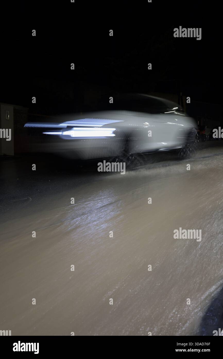 A fast-moving white vehicle captured at night with visible motion blur ...