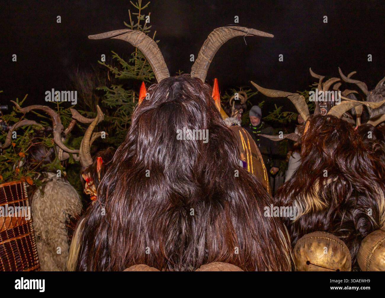 A group of Krampus figures in traditional costumes walk through a snowy ...