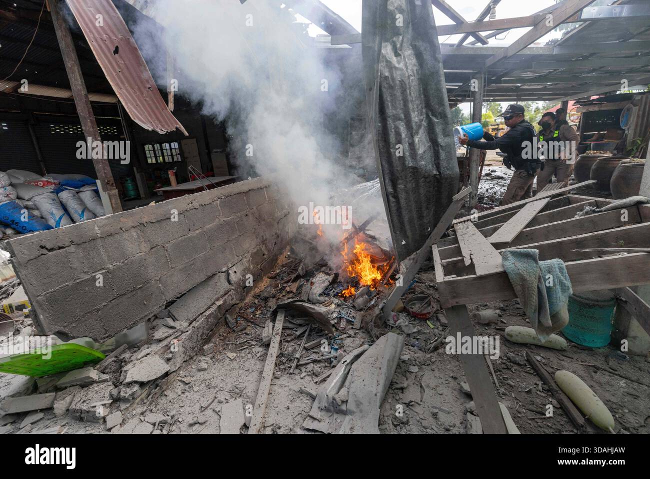 A Thai police officer splashes water to control fire at a house which ...