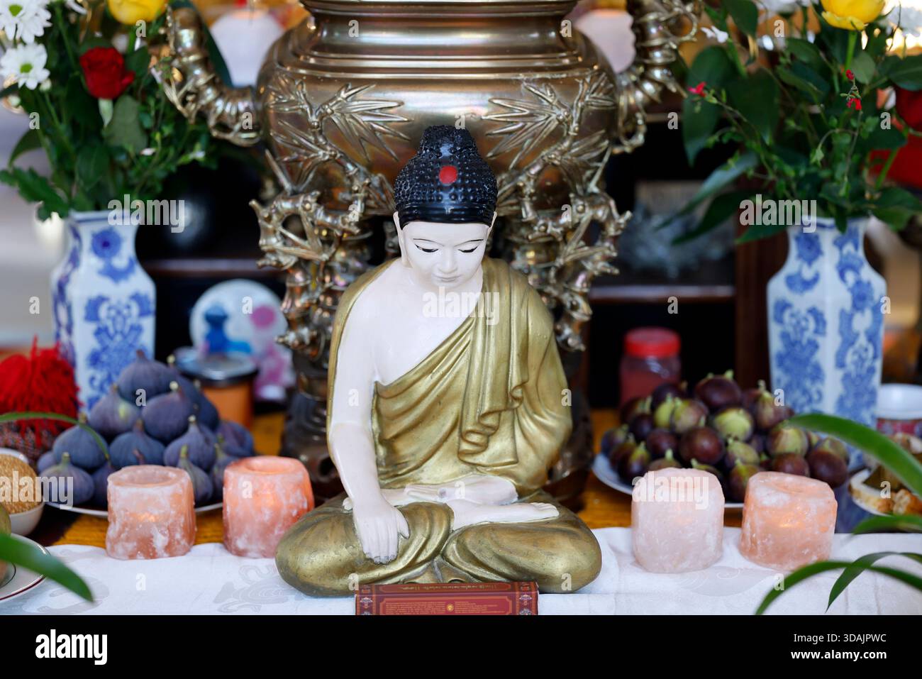 Buddha statue dressed in golden robe sits on altar, surrounded by ...