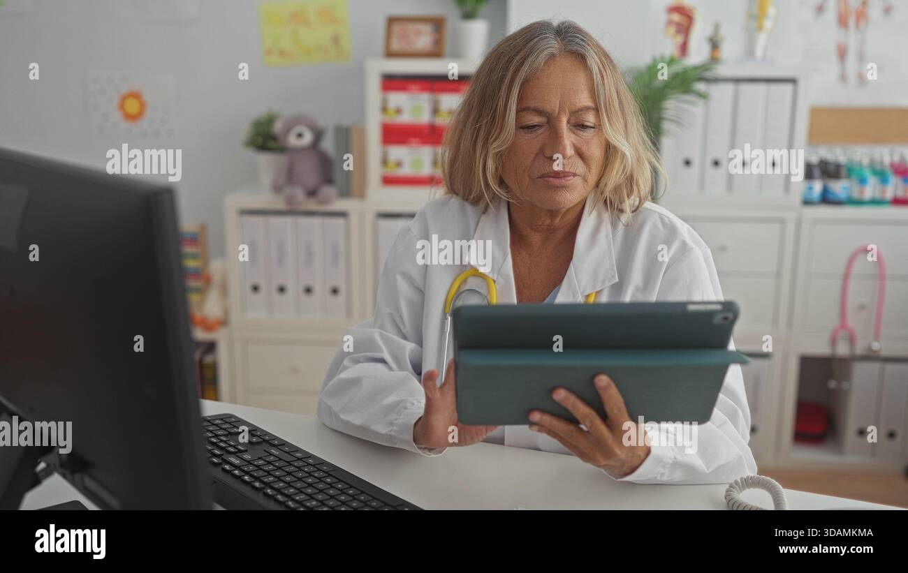 Senior woman pediatrician holds tablet and taps screen while typing at ...