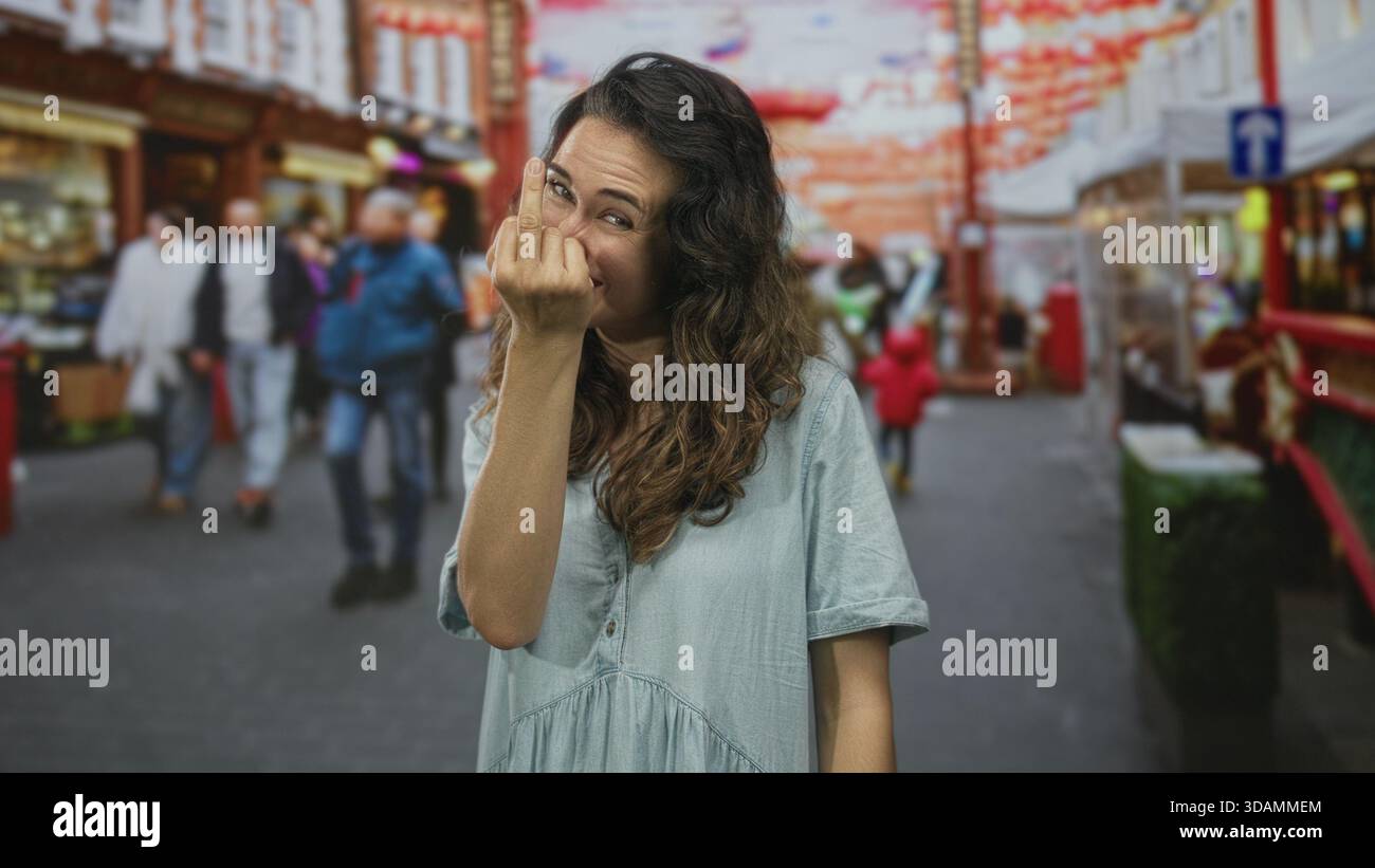 Young hispanic woman in denim dress grins and shows middle finger on ...