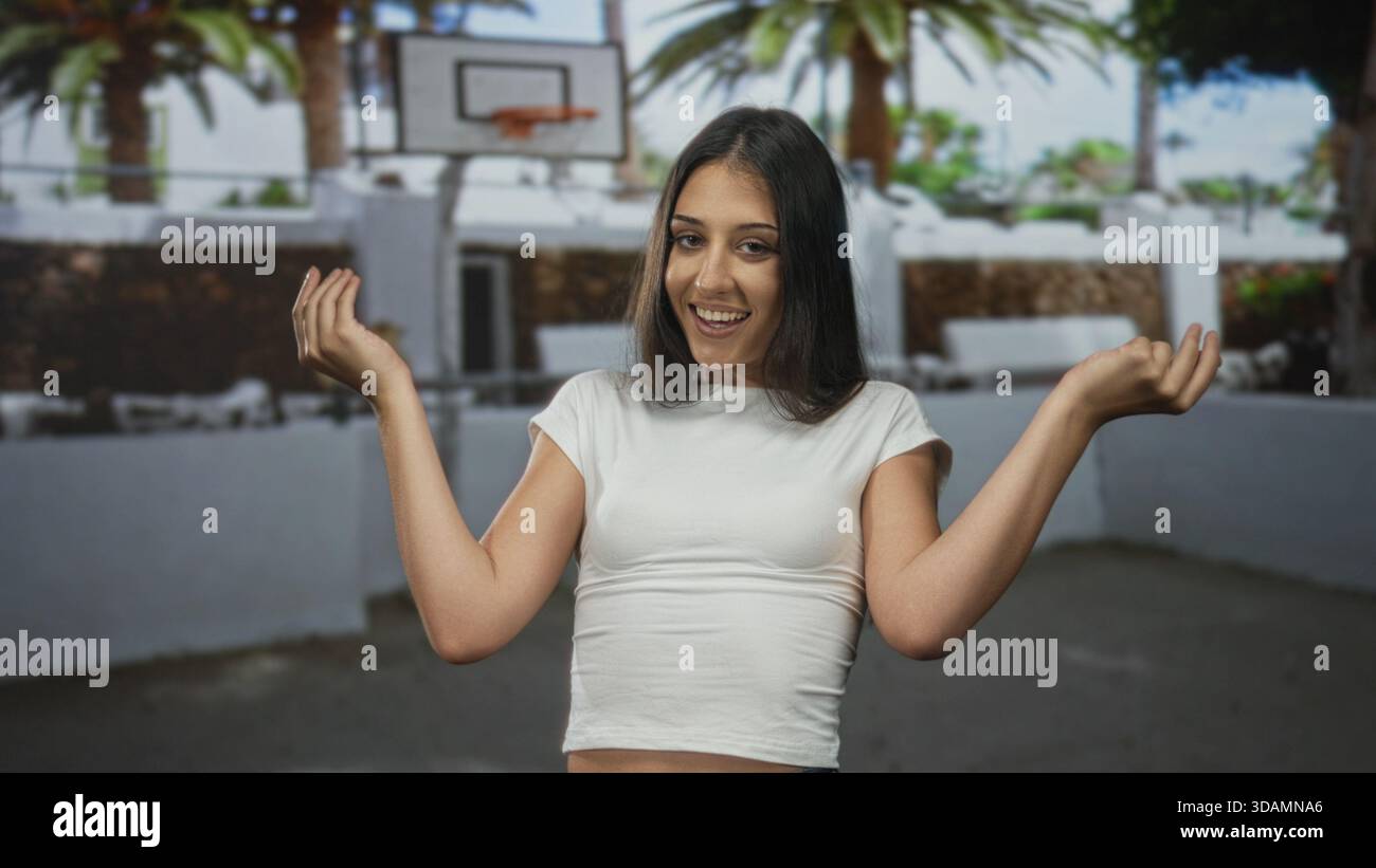 Woman shrugging with arms raised, wearing a white crop top on a street ...