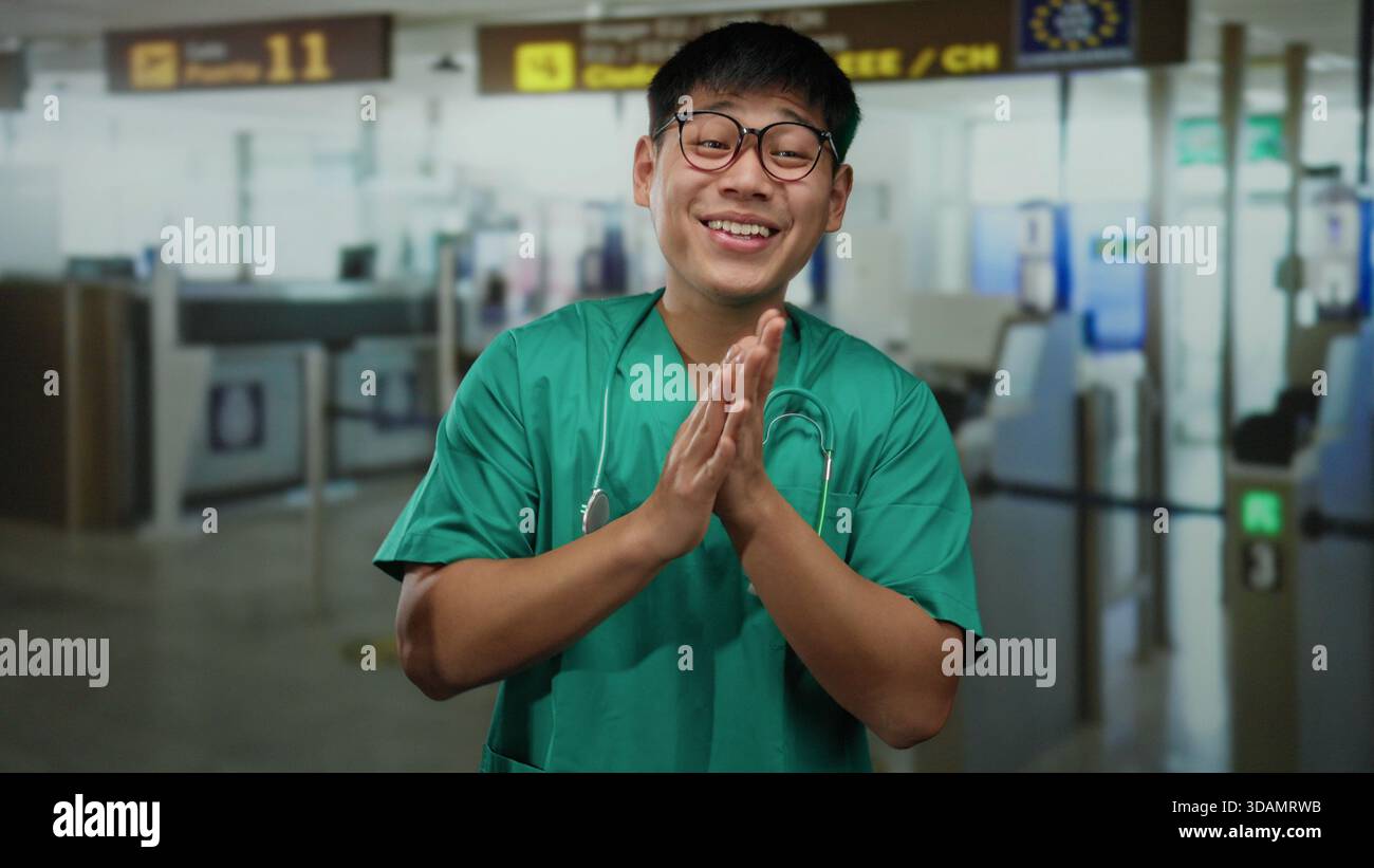 Young chinese man in green medical scrubs clapping at an airport ...