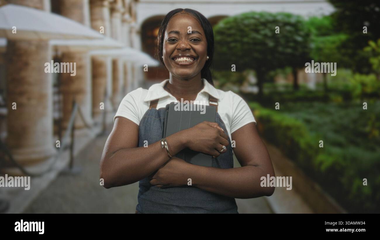 Woman in apron hugs tablet close with arms crossed over device, smiling ...