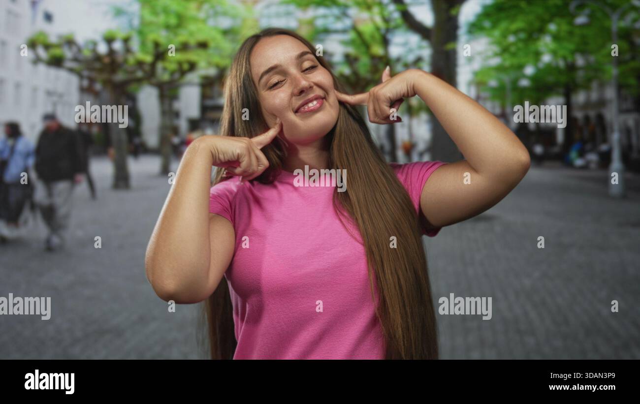 Woman points finger to cheeks and puffs cheeks on street in pink t ...