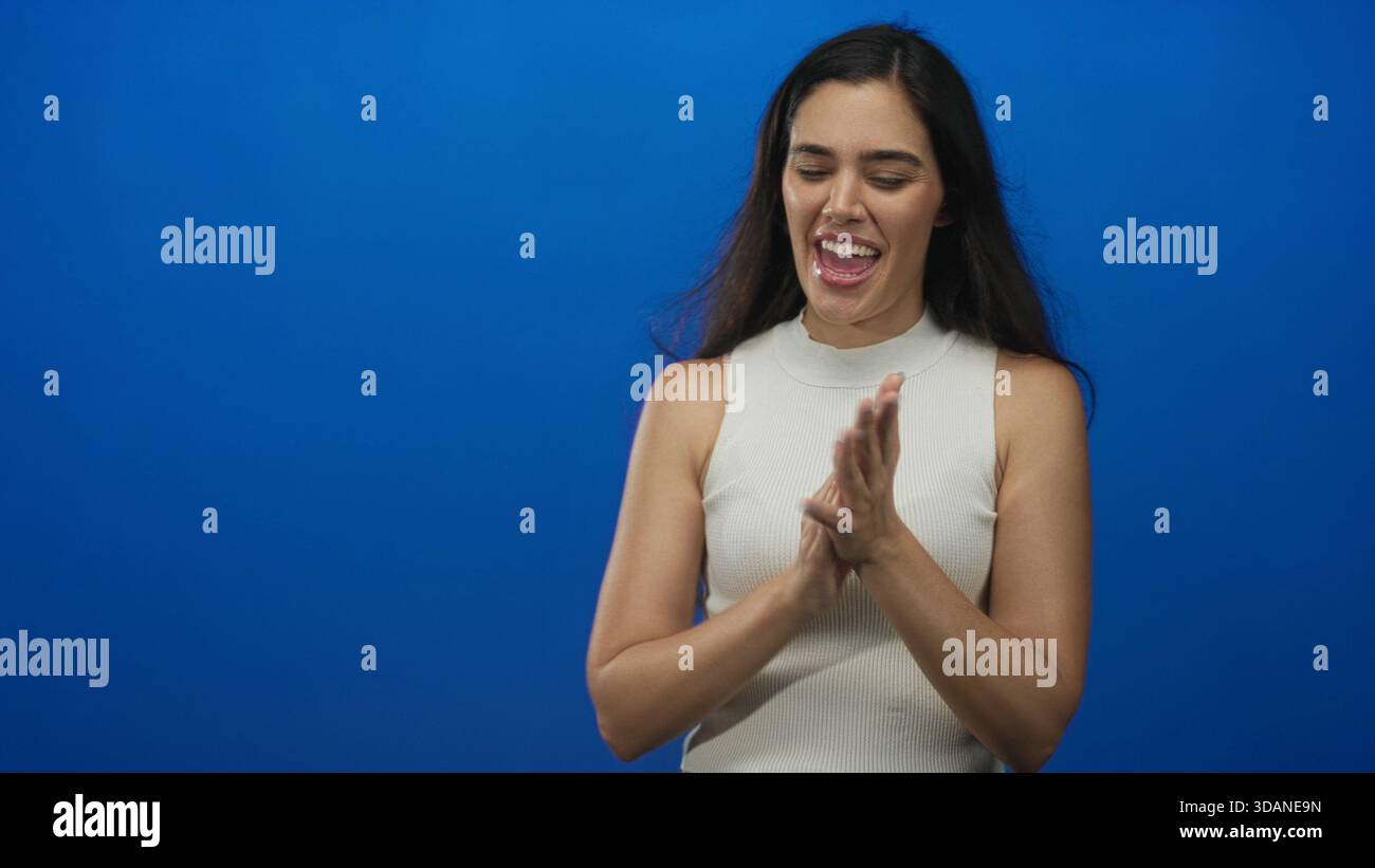 Young woman clapping hands with open smile in studio against bold blue ...
