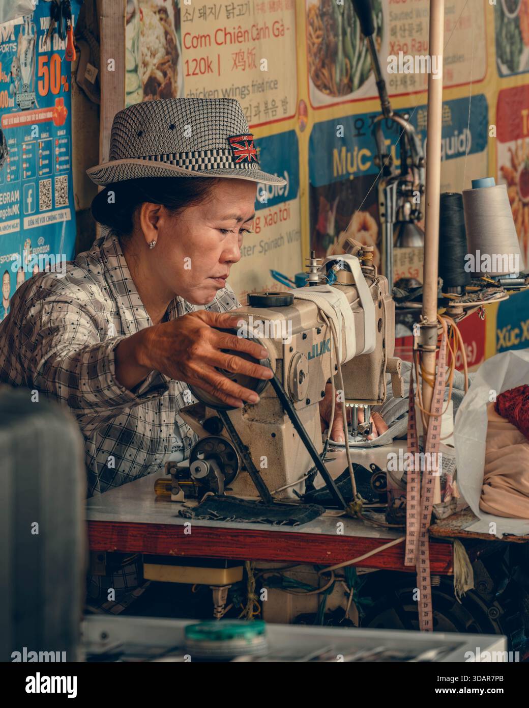 A focused shot of an elderly Asian woman in a hat operating an ...