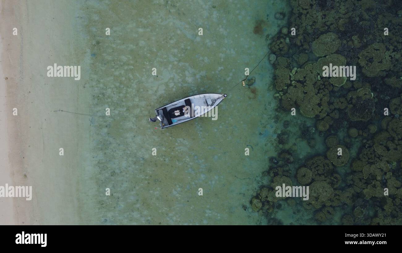 Drone image of small boat anchored between sandy beach and coral reef ...