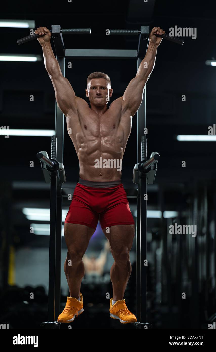 muscular athlete is doing pull ups on a bar in the gym. He focuses on ...