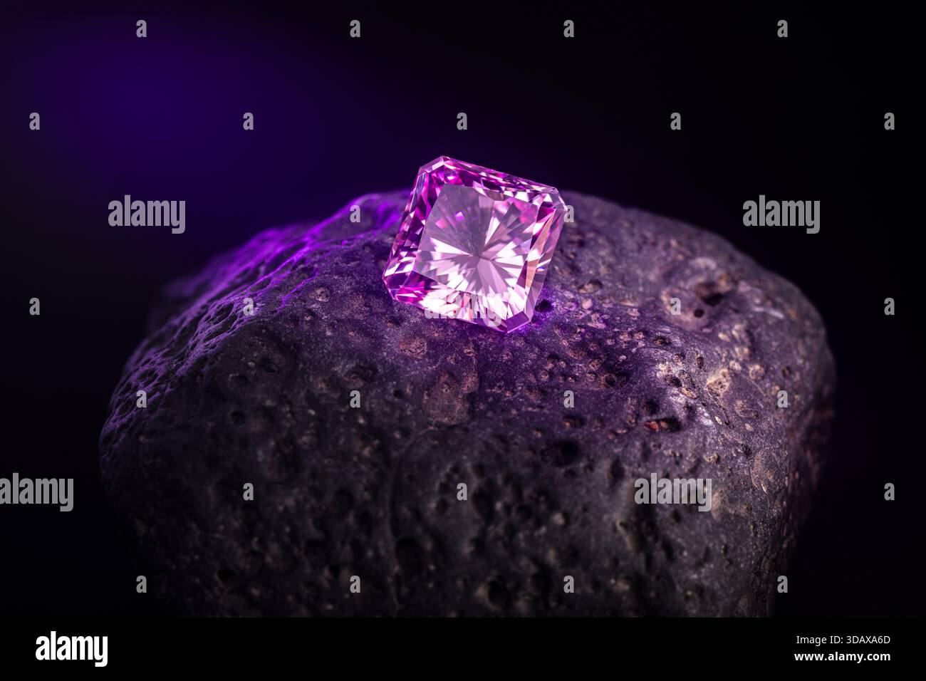 A small pink diamond is sitting on a rock. The rock is dark and the ...