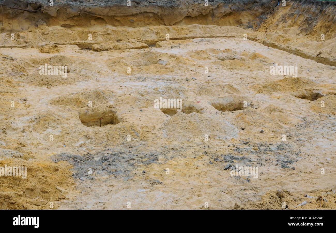 Workers prepare construction site with several dug holes in sand for ...