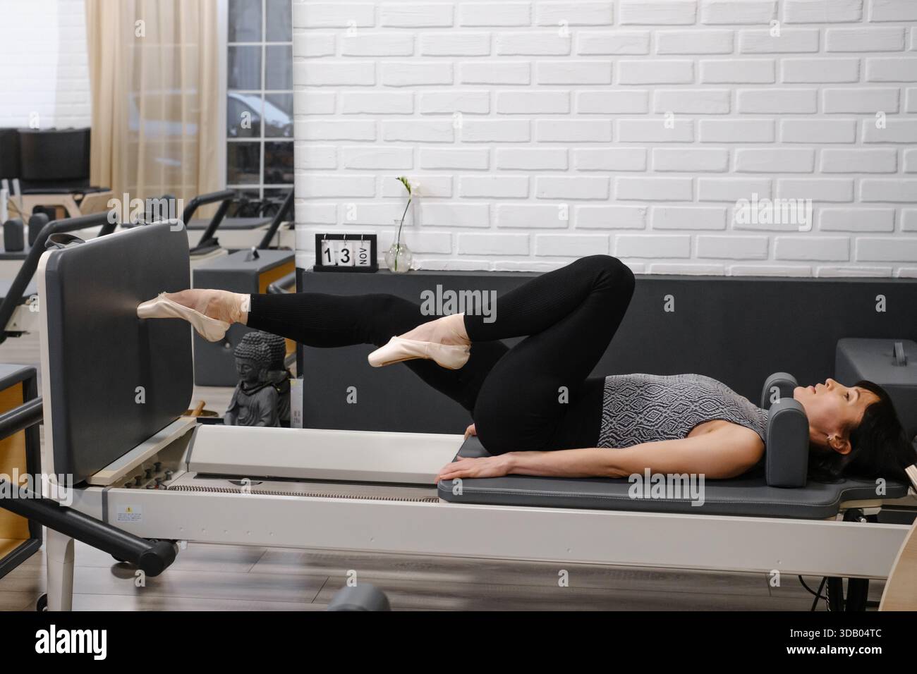 Woman performing pilates reformer exercise in ballet pointe shoes ...