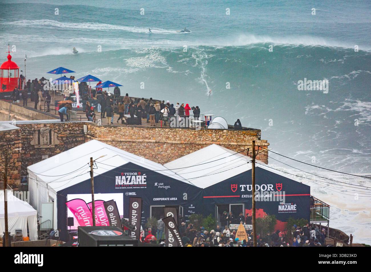 A surfer rides a towering wave off Praia do Norte as spectators crowd ...