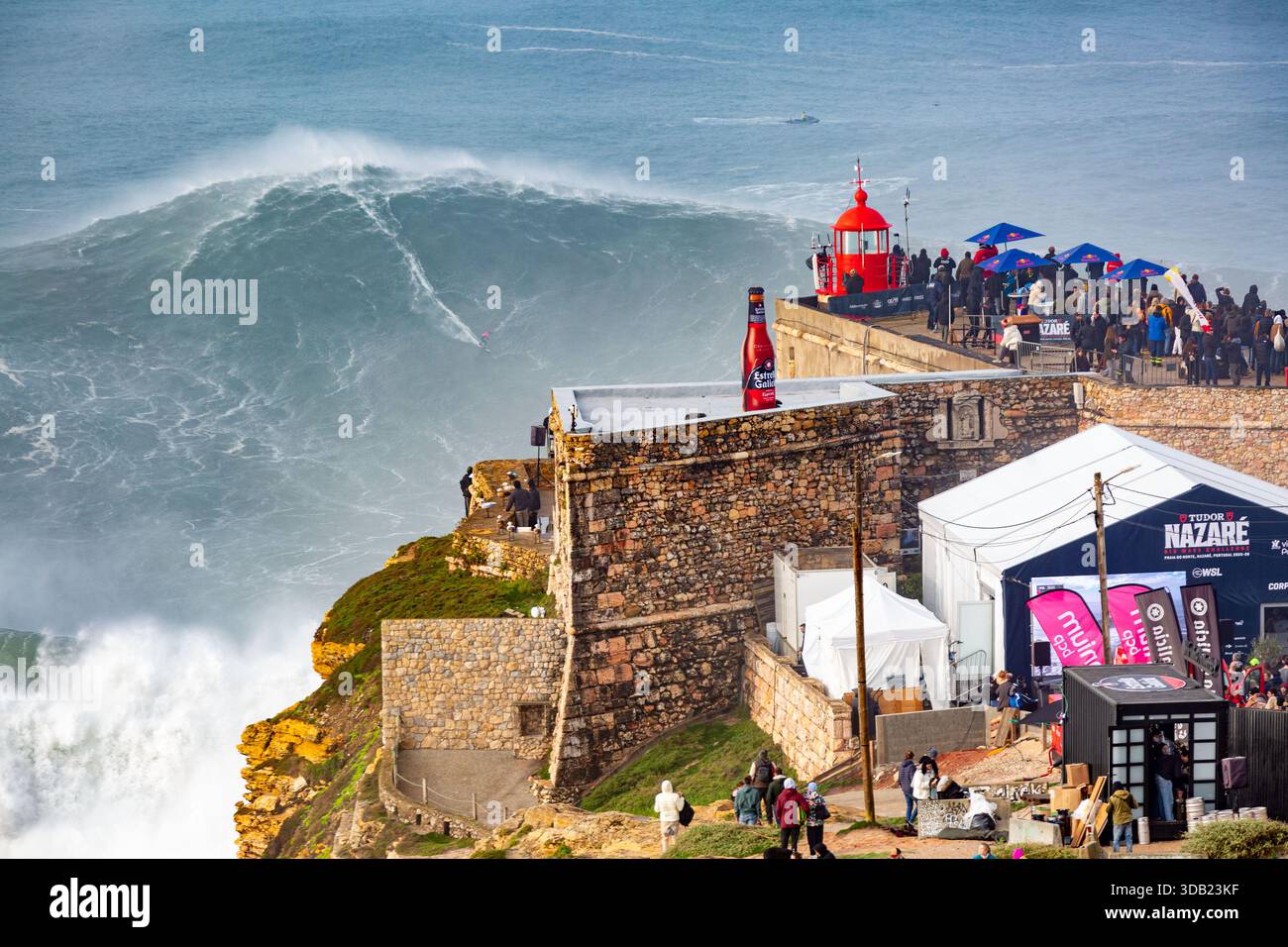 A surfer rides a towering wave off Praia do Norte as spectators crowd ...