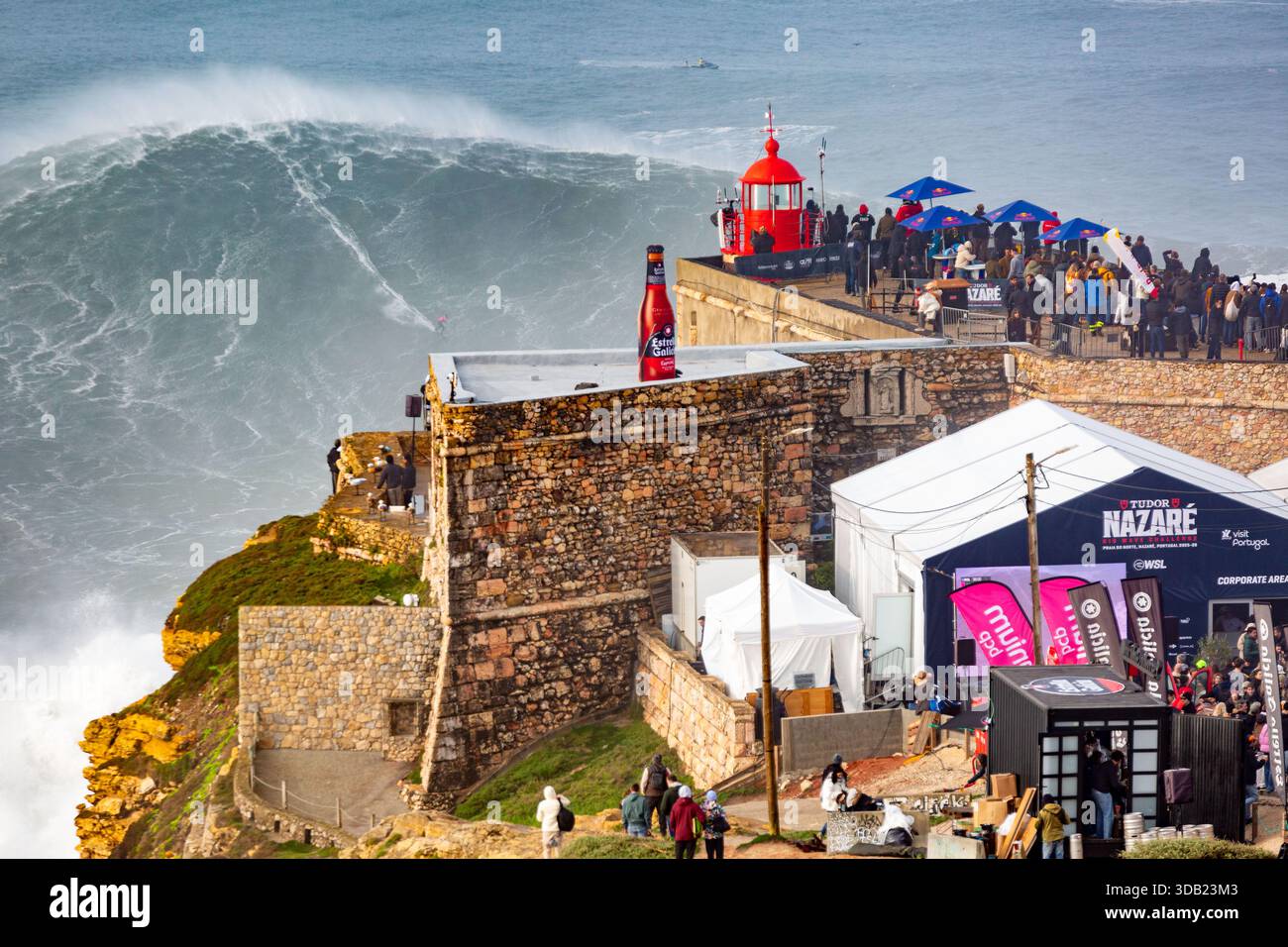 A surfer rides a towering wave off Praia do Norte as spectators crowd ...
