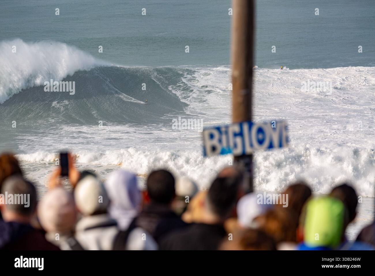 A surfer rides a massive wave as spectators capture the moment during ...