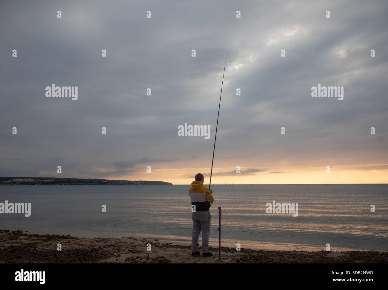 13 December 2025, Spain, Palma: Matias fishing with a rod on the Arenal ...
