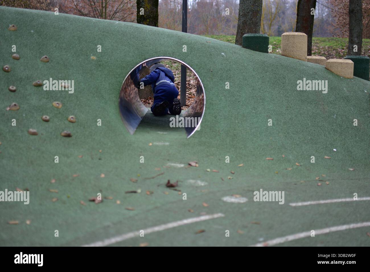 Toddler crawling through a metal tunnel built into a playground hill ...