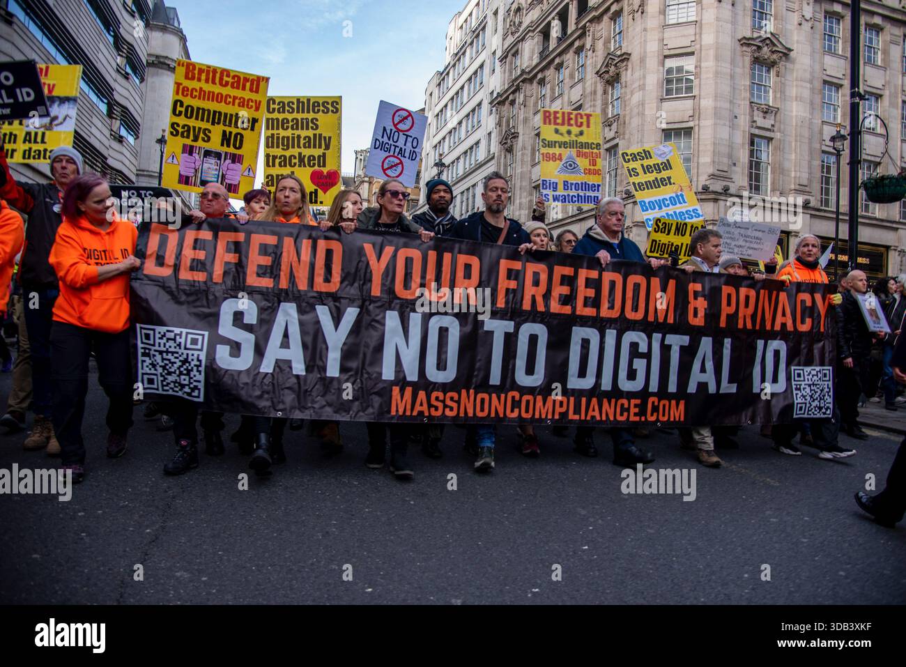 Protestors hold a large banner and placards during the "Say No To ...