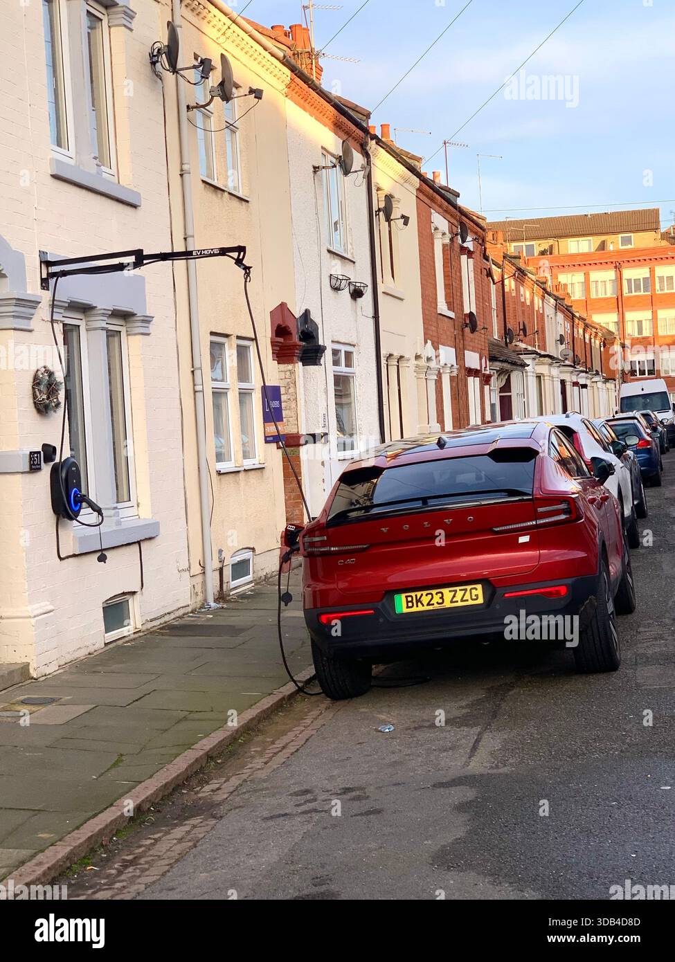 red electric vehicle charging outside terraced house using a cable from ...