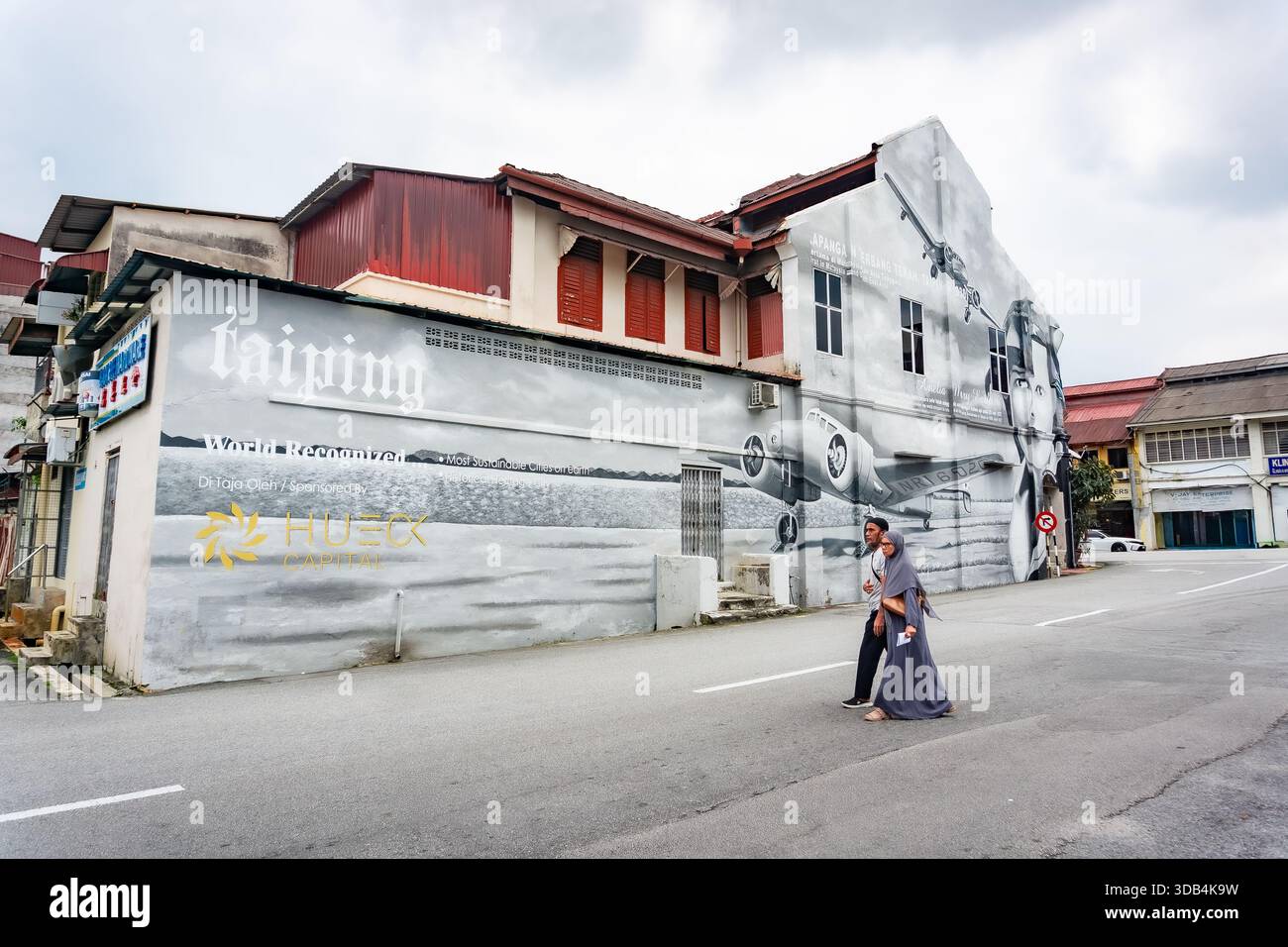A couple walks past a large heritage mural in Taiping town, Perak ...