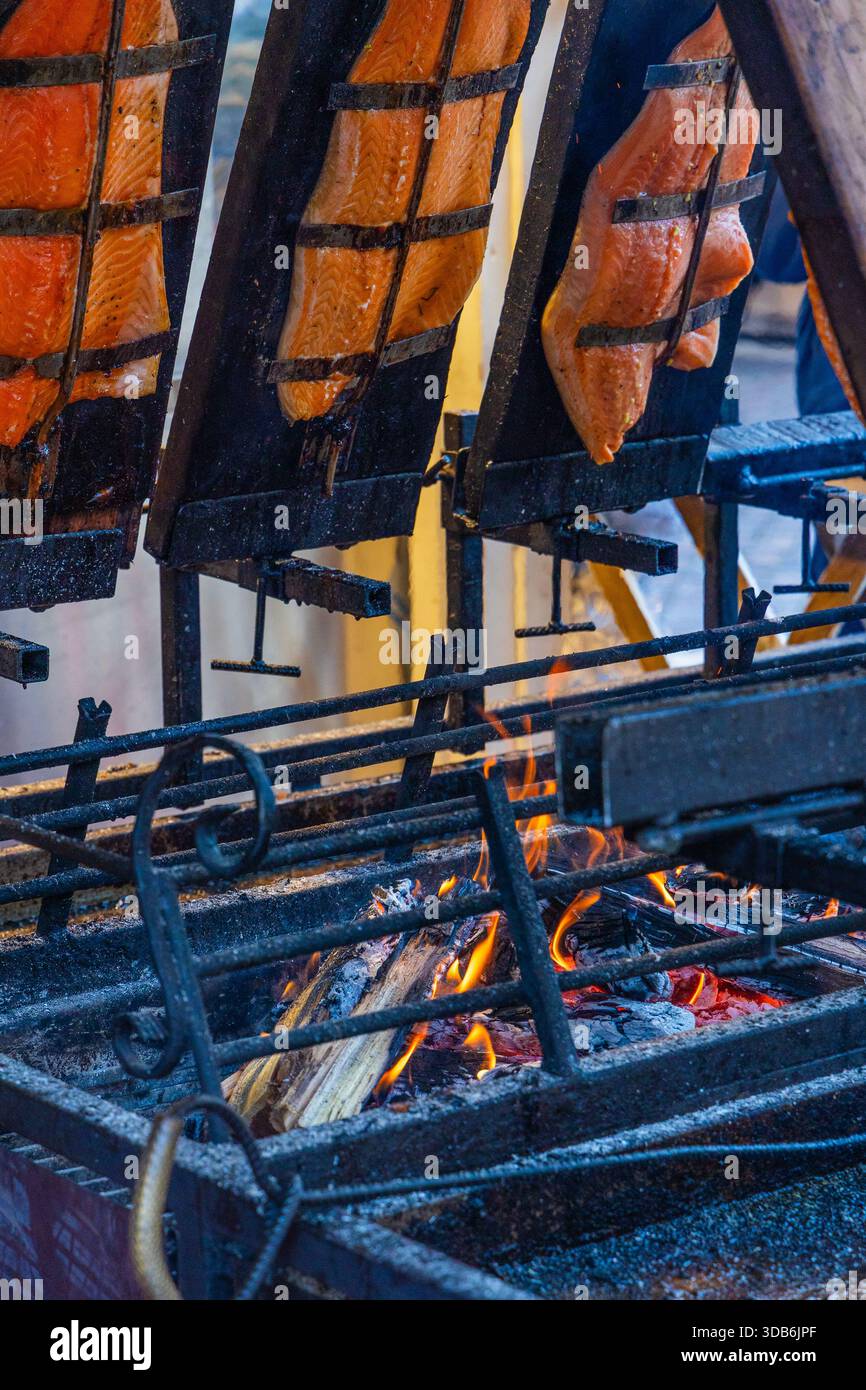 Thick salmon fillets are cooked vertically over an open wood fire at a ...