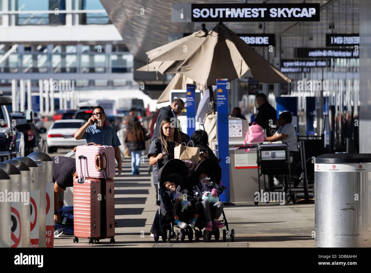 Travelers with luggage and a stroller move along the departures curb at ...