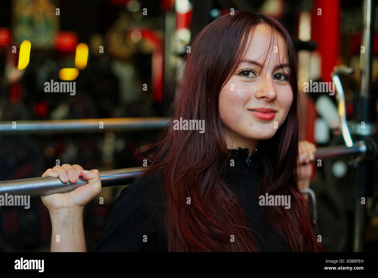 Young woman with determined smile holding a barbell across her ...