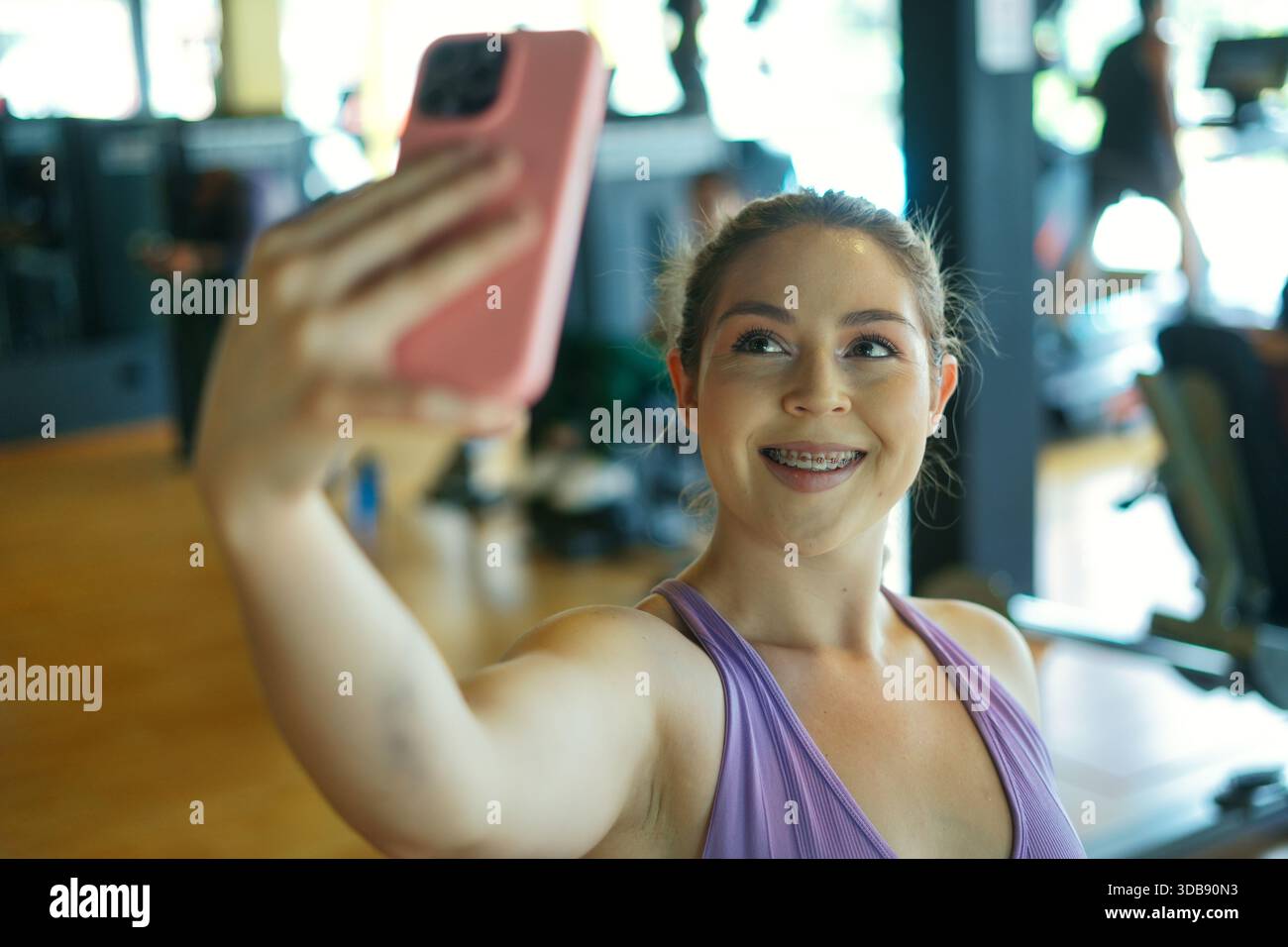Young woman with braces smiling confidently into her smartphone after a ...