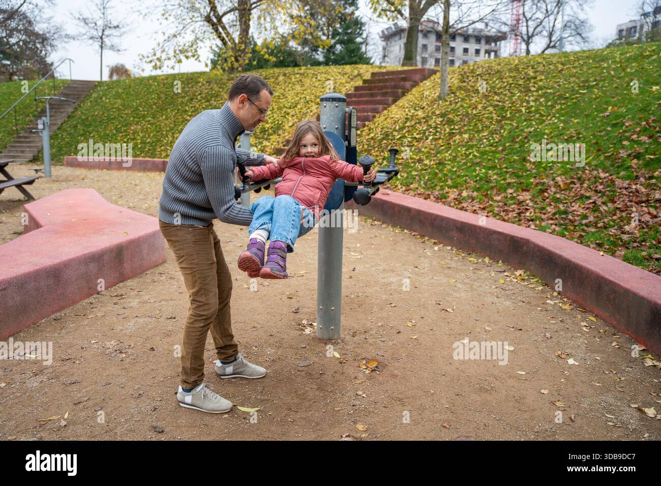 Father helping daughter to play on a playground rotating machine ...