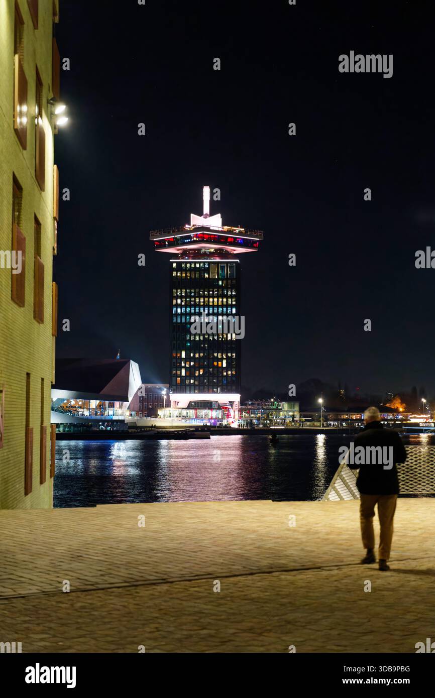 A person walks along a waterfront promenade at night in an urban ...