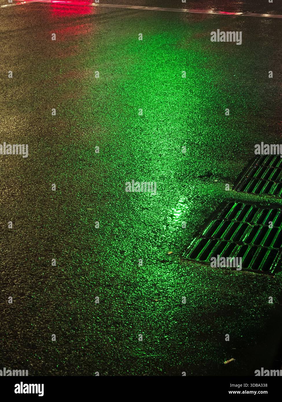 Wet asphalt street reflecting vibrant green and subtle red lights ...