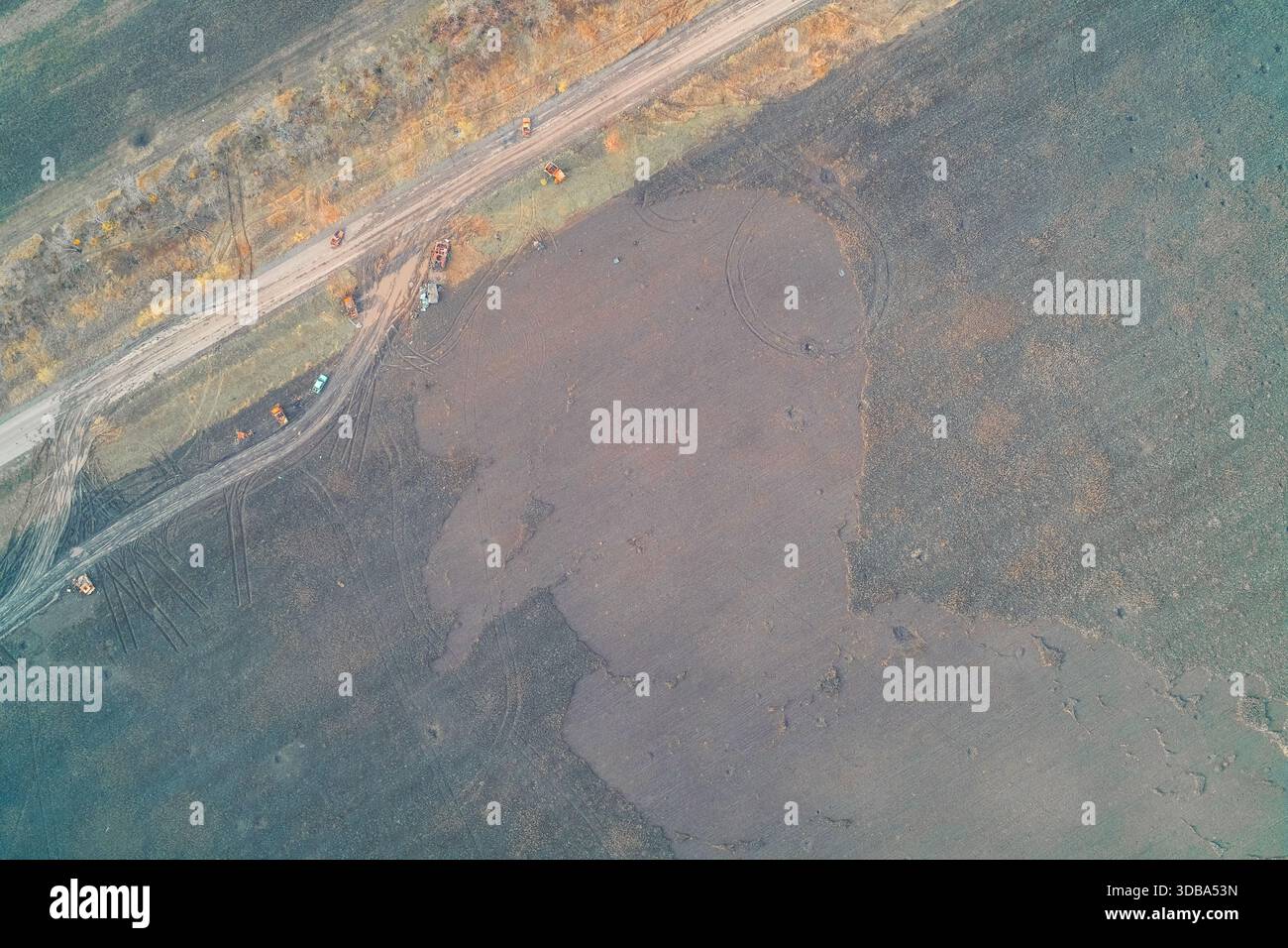 Top-down aerial view of a dirt road next to a heavily scorched field ...