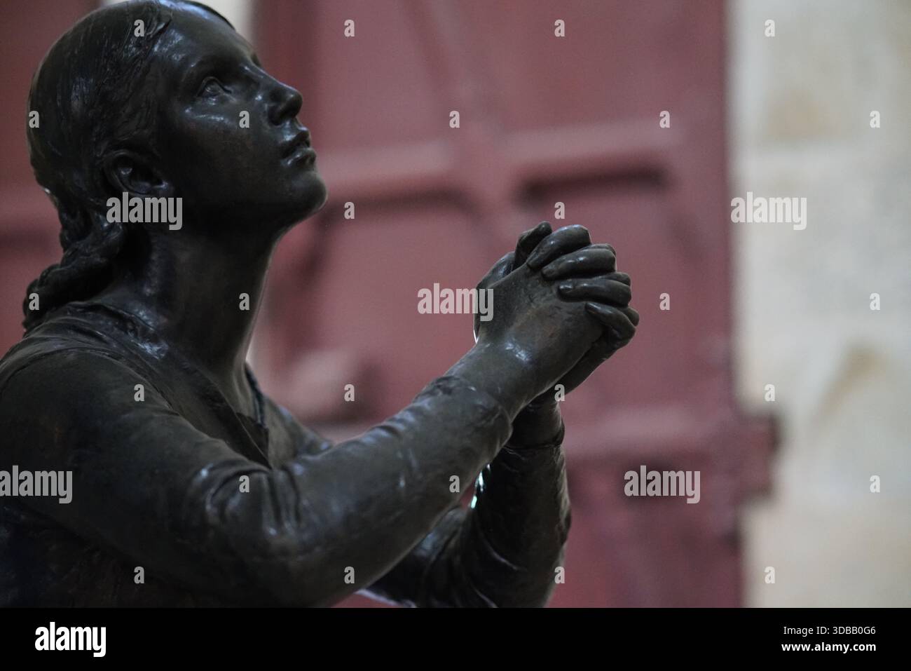 Bronze statue of a praying figure with clasped hands inside a church in ...