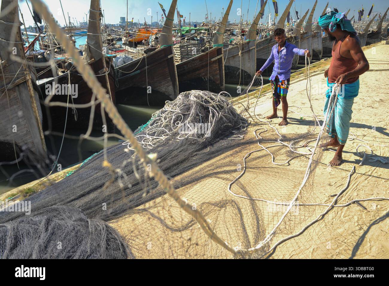 Fishermen mend and repair their fishing nets on the bank of the ...