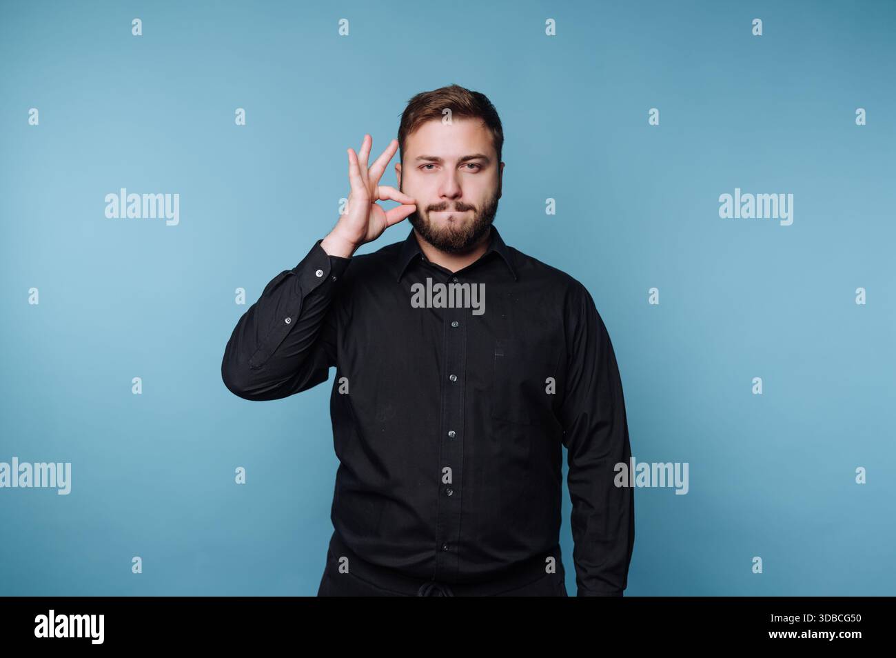 A man stands in front of a blue wall. He shows a hand gesture with one ...