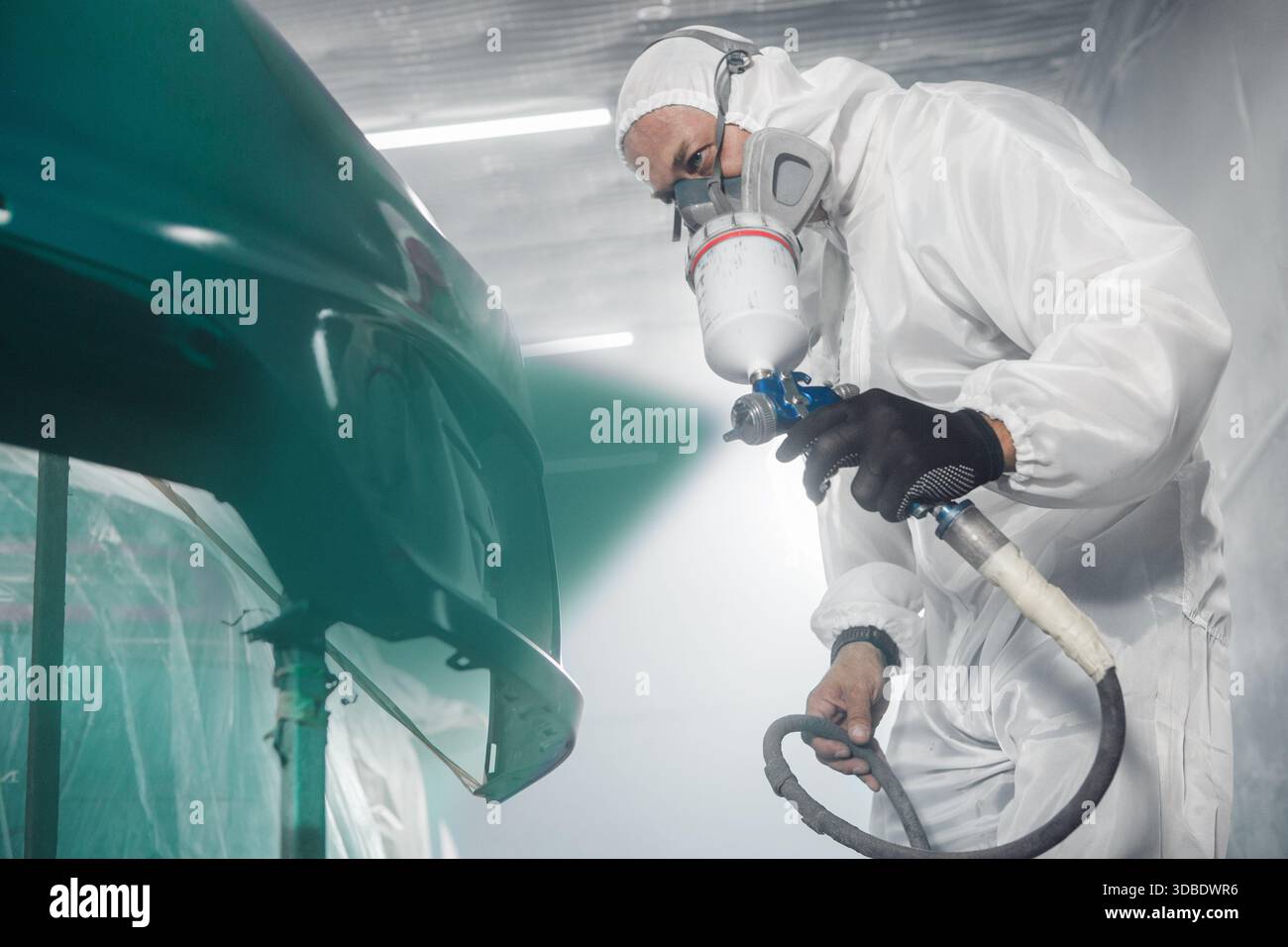 Car paint worker spraying green paint to car body element using spray ...