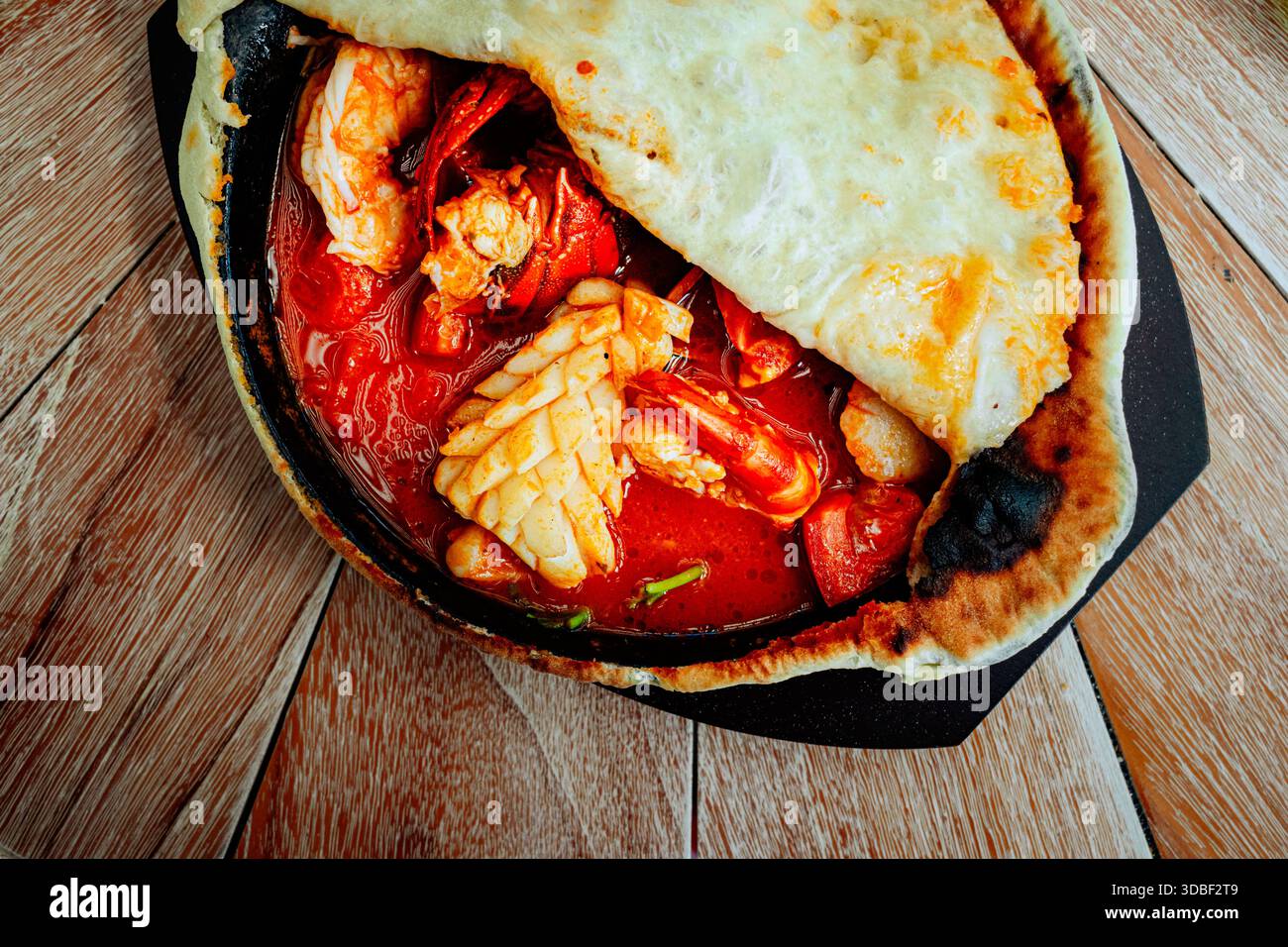 A seafood stew en croute, featuring prawns, squid, and crab, simmers in ...