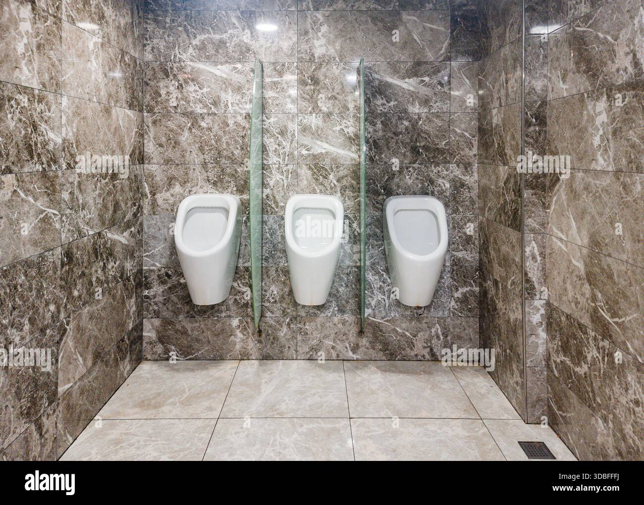 Minimalist public men's restroom with three white urinals separated by ...