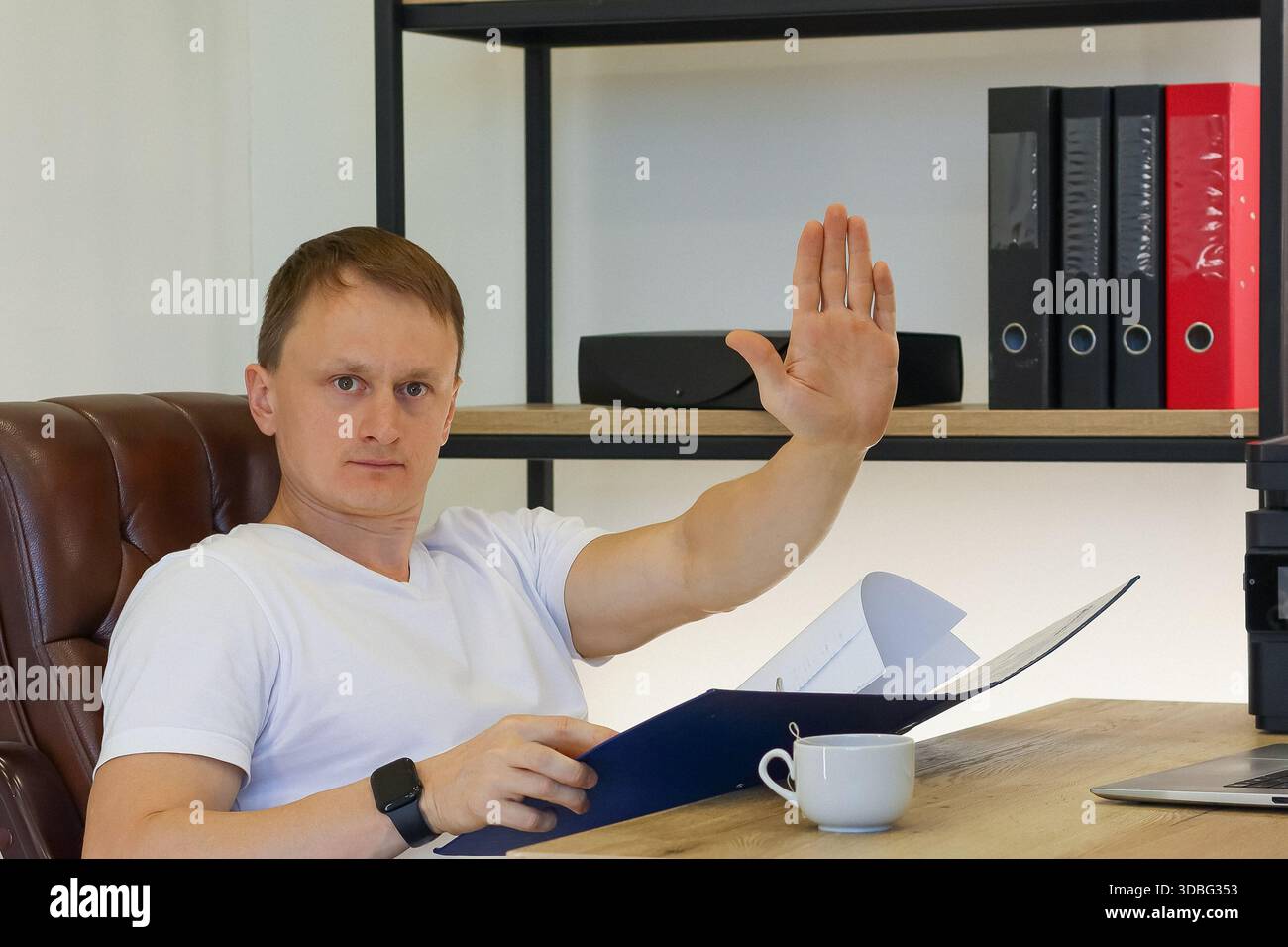 Young adult male in white shirt sitting at desk, arm raised with open ...