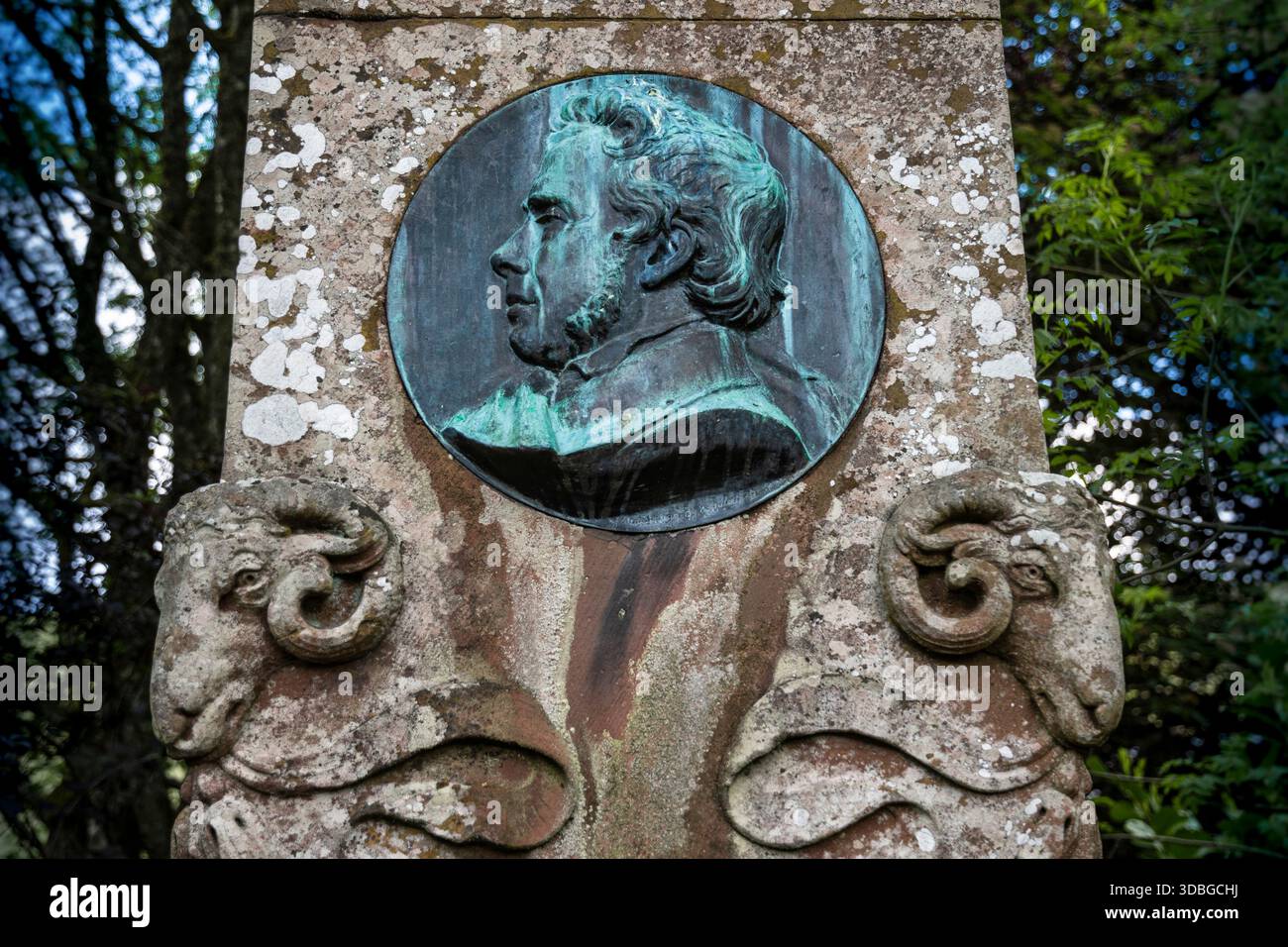 A weathered memorial statue with bronze portrait plaque in a mossy ...