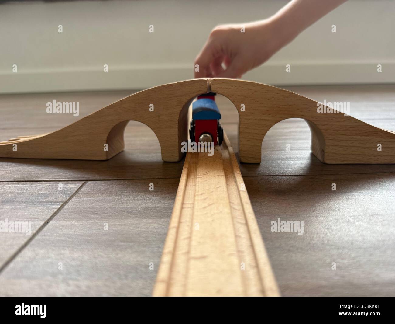 child's hand pushes wooden toy train under bridge, floor, concept of ...