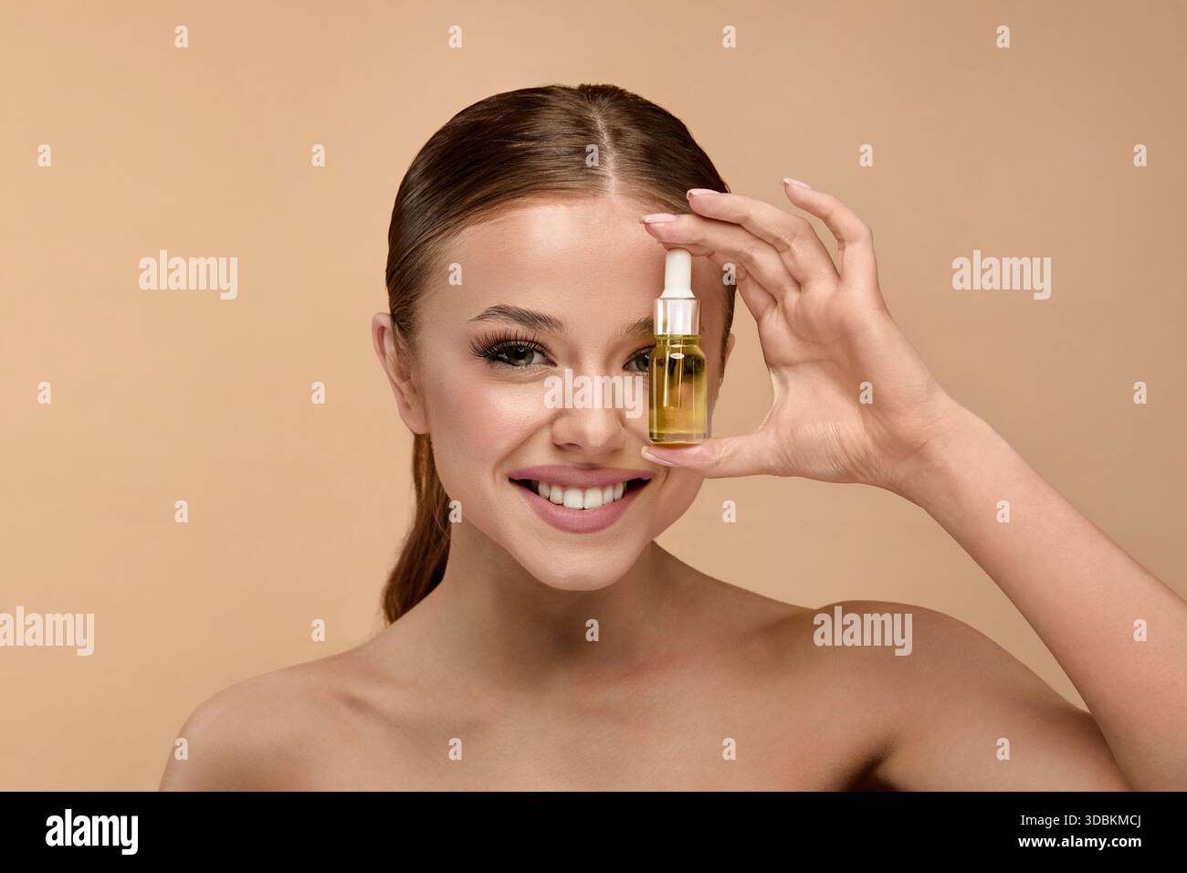 Woman poses in studio holding serum for skincare treatment. She smiles ...