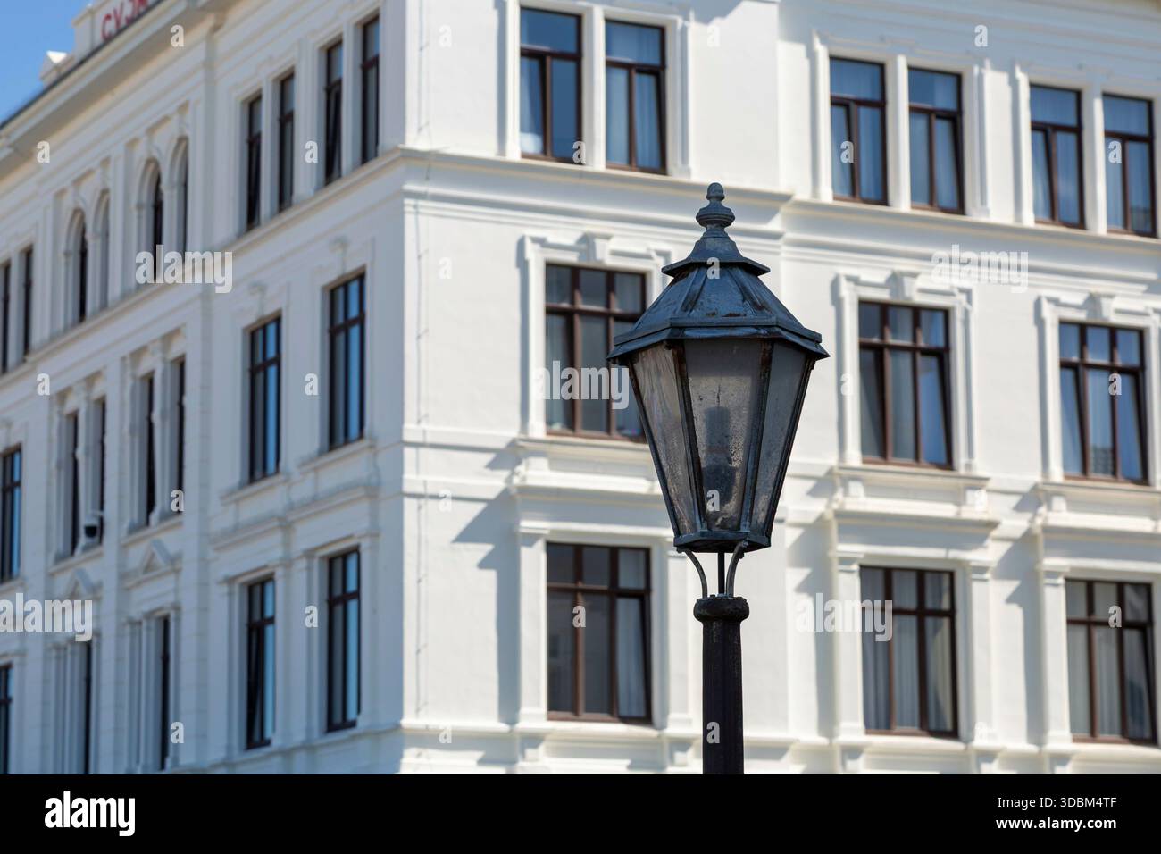 A black street lamp stands in front of a white building with dark ...