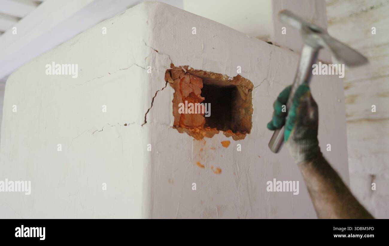 Construction worker breaking white wall with hammer revealing bricks ...