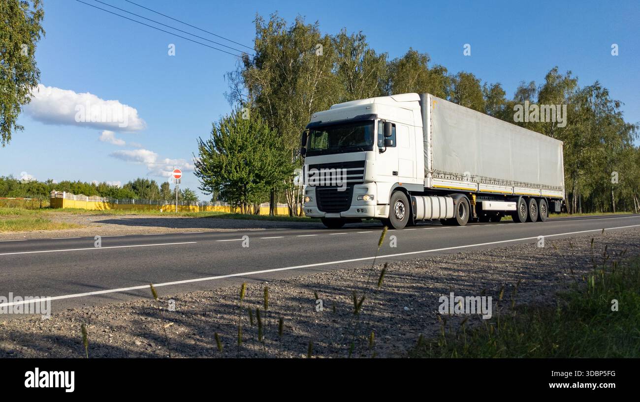 White semi-truck with a fully loaded cargo trailer driving along ...