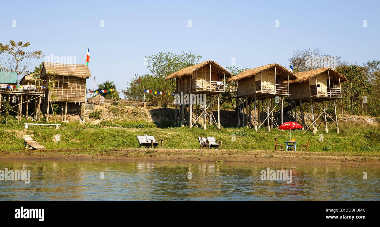 Traditional wooden eco lodges on stilts along a riverbank in Chitwan ...