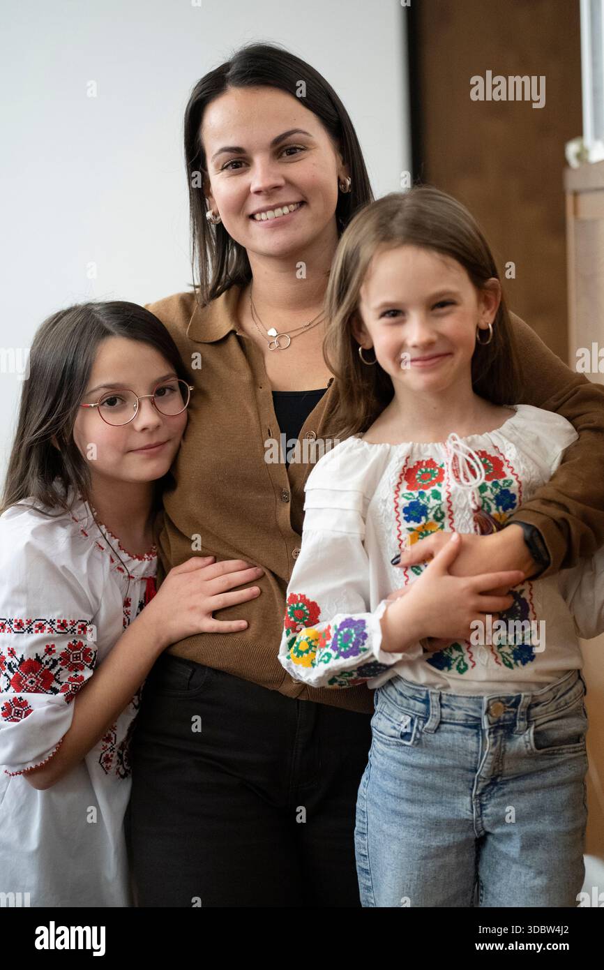 Vertical photo of loving mother hugging two daughters in vyshyvankas ...