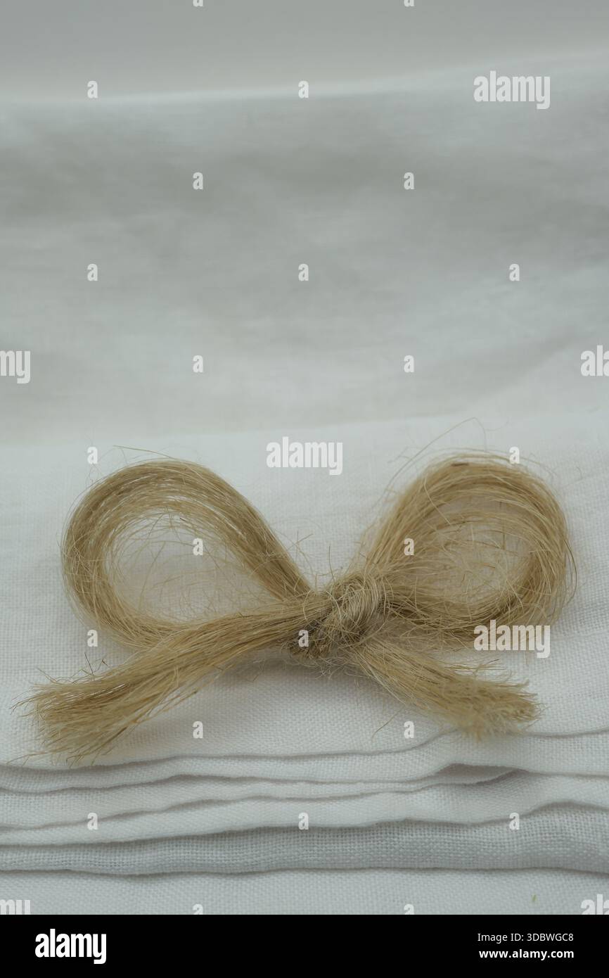Flax fiber filament in the shape of a bow on folded snow-white linen ...